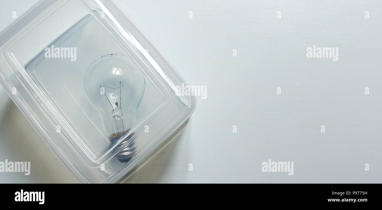 a light bulb inside clear box on white wooden surface, think inside a ...