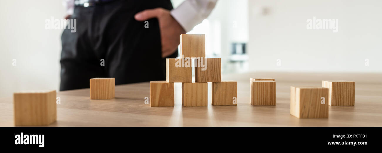 Wooden cubes stacked in pyramid on office desk with businessman ...