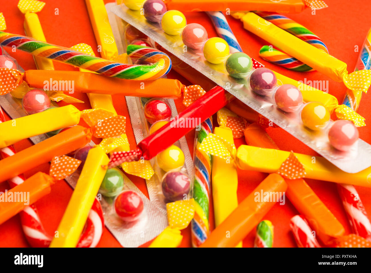Different candies in packs on red background Stock Photo - Alamy
