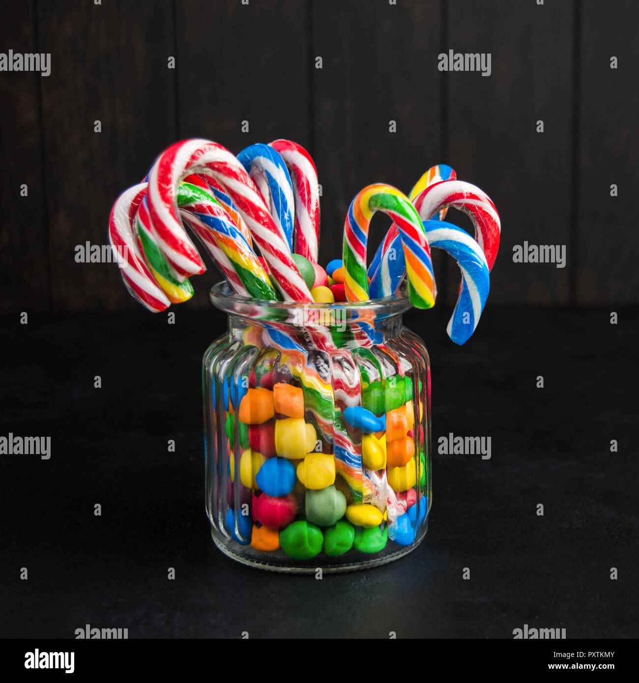 Colorful candy canes with sweets in glass jar over black background ...