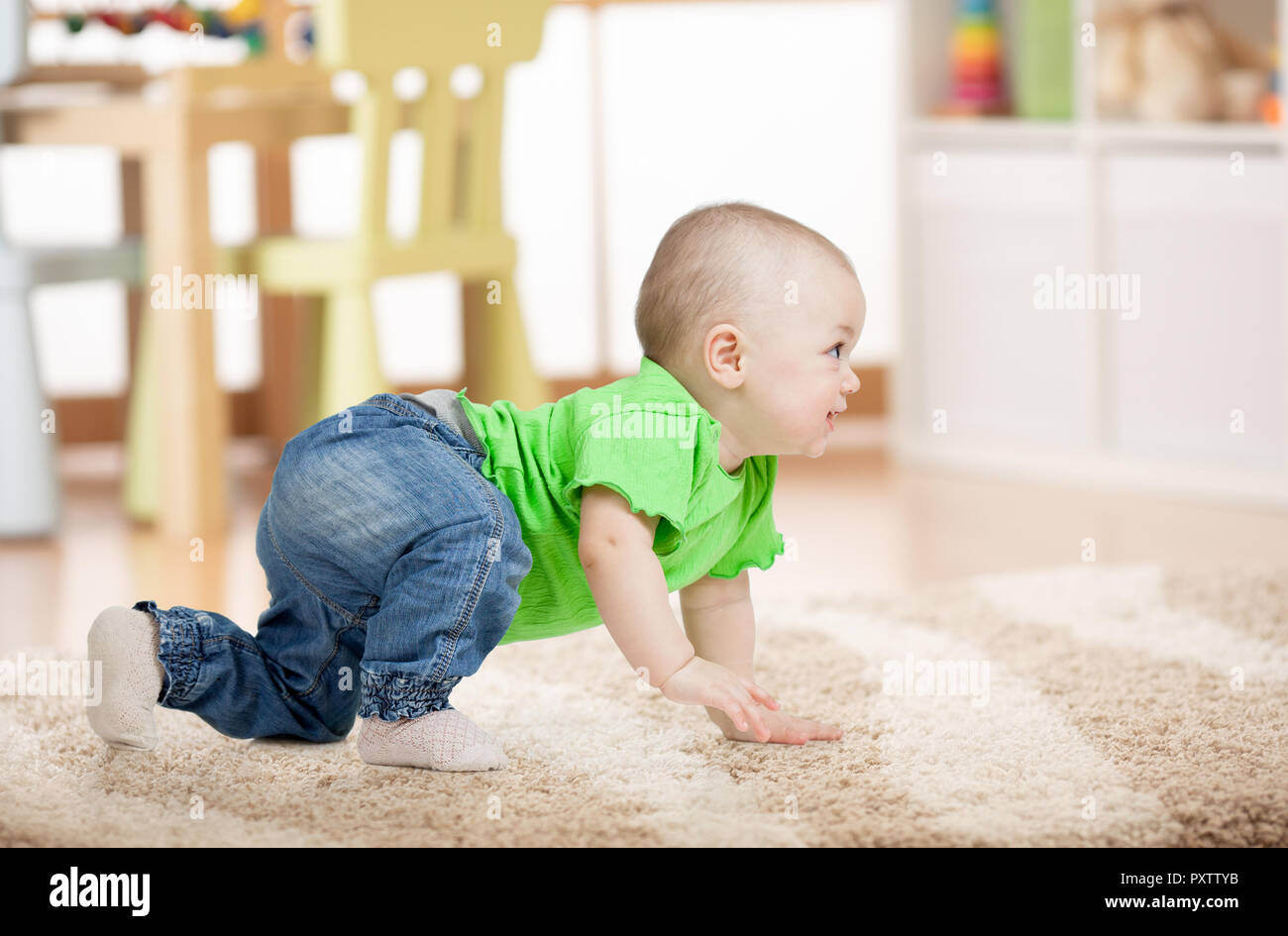 side view of baby crawling on soft carpet on floor in children room ...