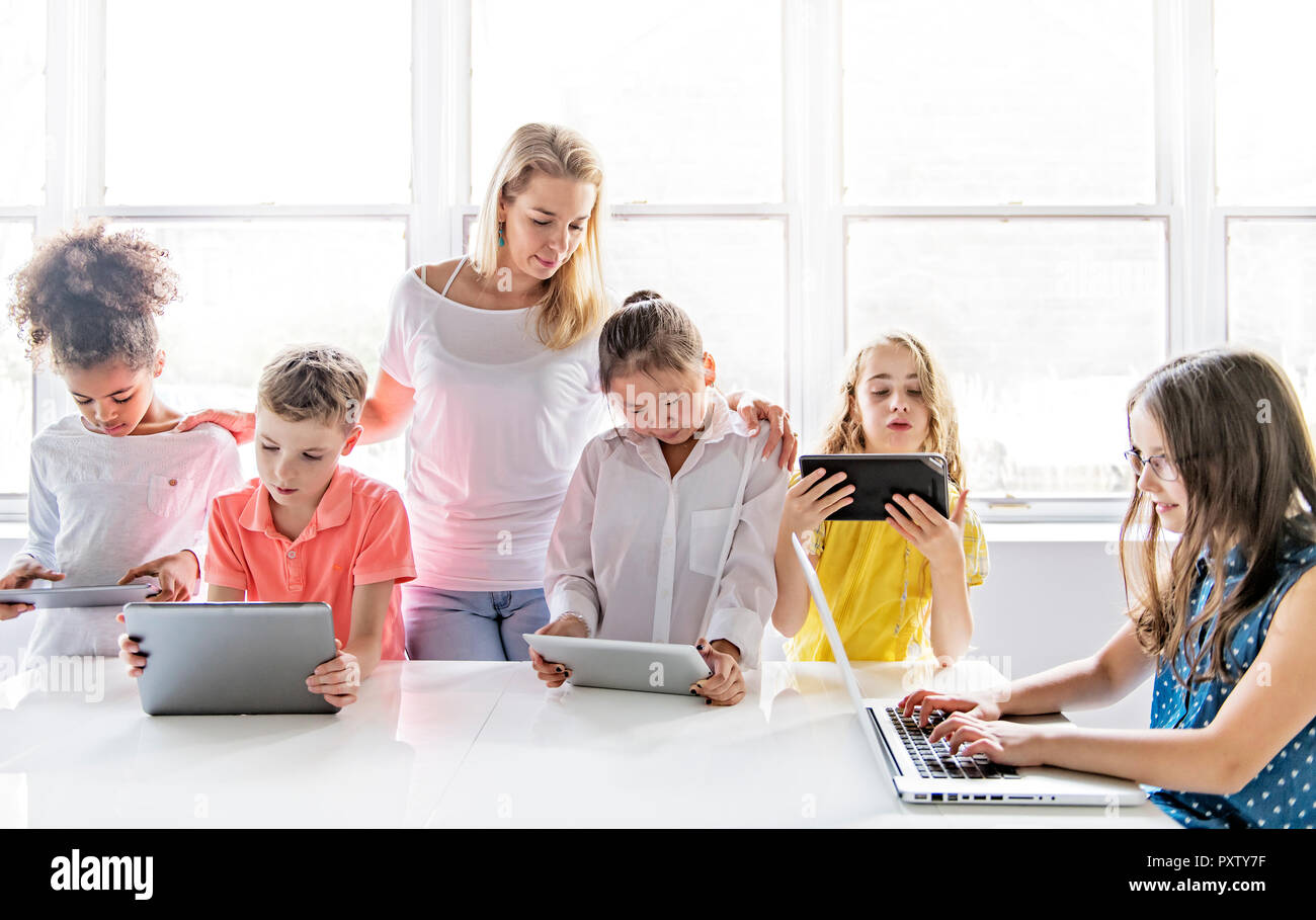 A child with technology tablet and laptop computer in classroom teacher ...