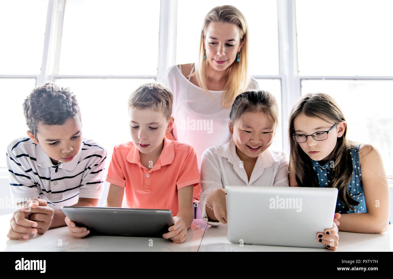 A child with technology tablet and laptop computer in classroom teacher ...