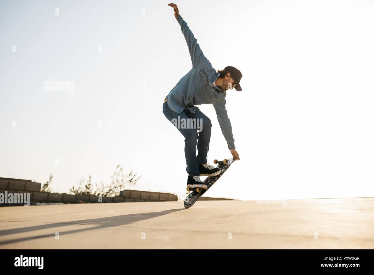 Trendy man in denim and cap skateboarding, standing on skateboard Stock ...