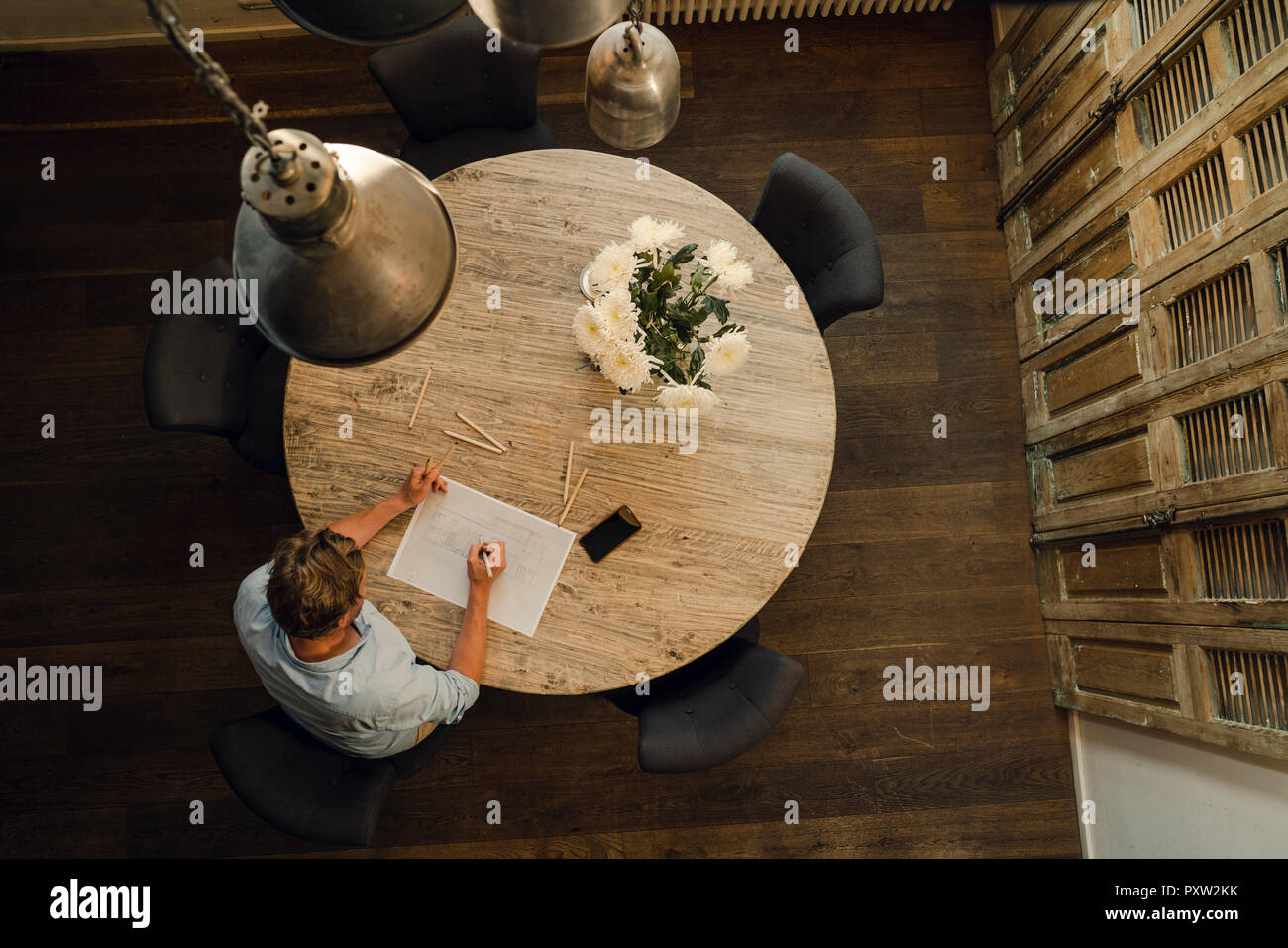 Mature man sitting at a round table, drawing with coloured pencils ...