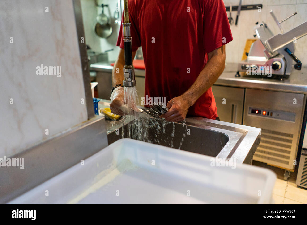 Man washing cutlery over sink in restaurant kitchen Stock Photo - Alamy