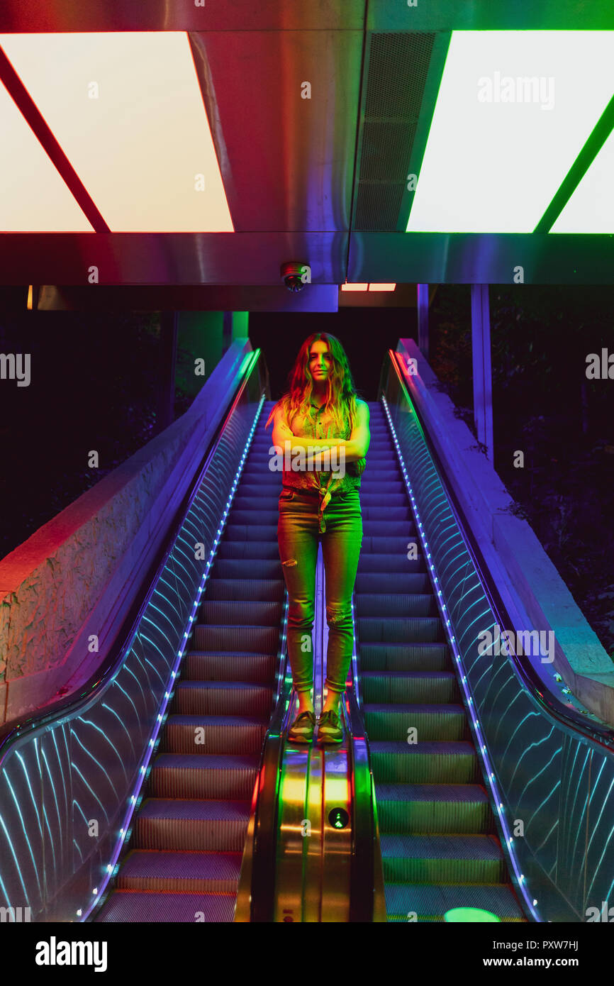Portrait of illuminated young woman standing on railing of escalator ...