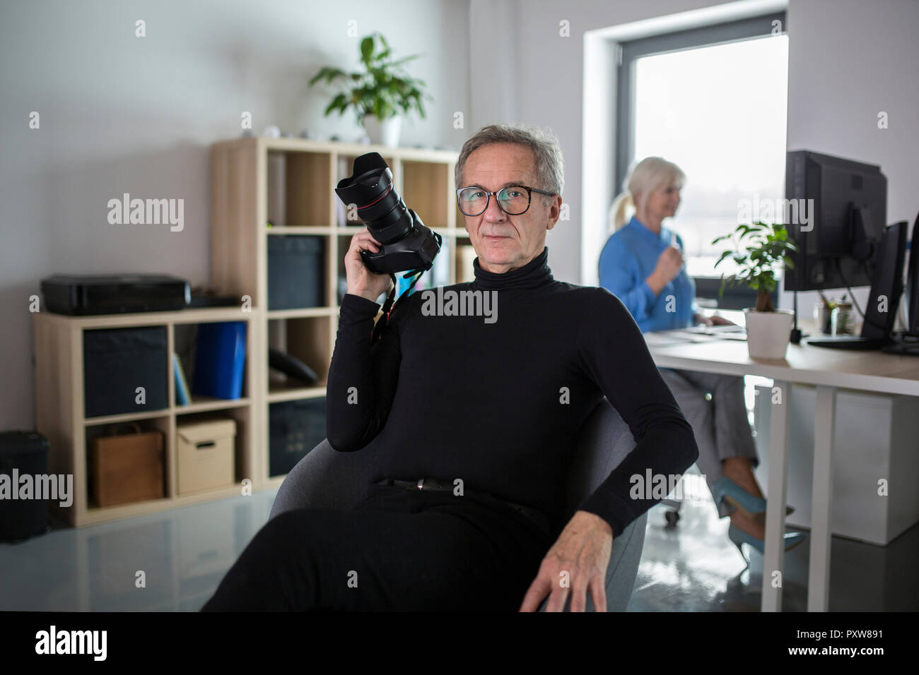 Senior man camera sitting office colleague working behind him hi-res ...