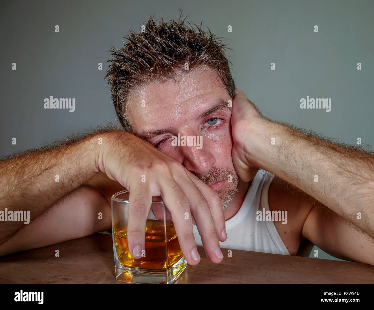 young drunk and pissed alcoholic man wasted wearing dirty singlet drinking whiskey glass ...