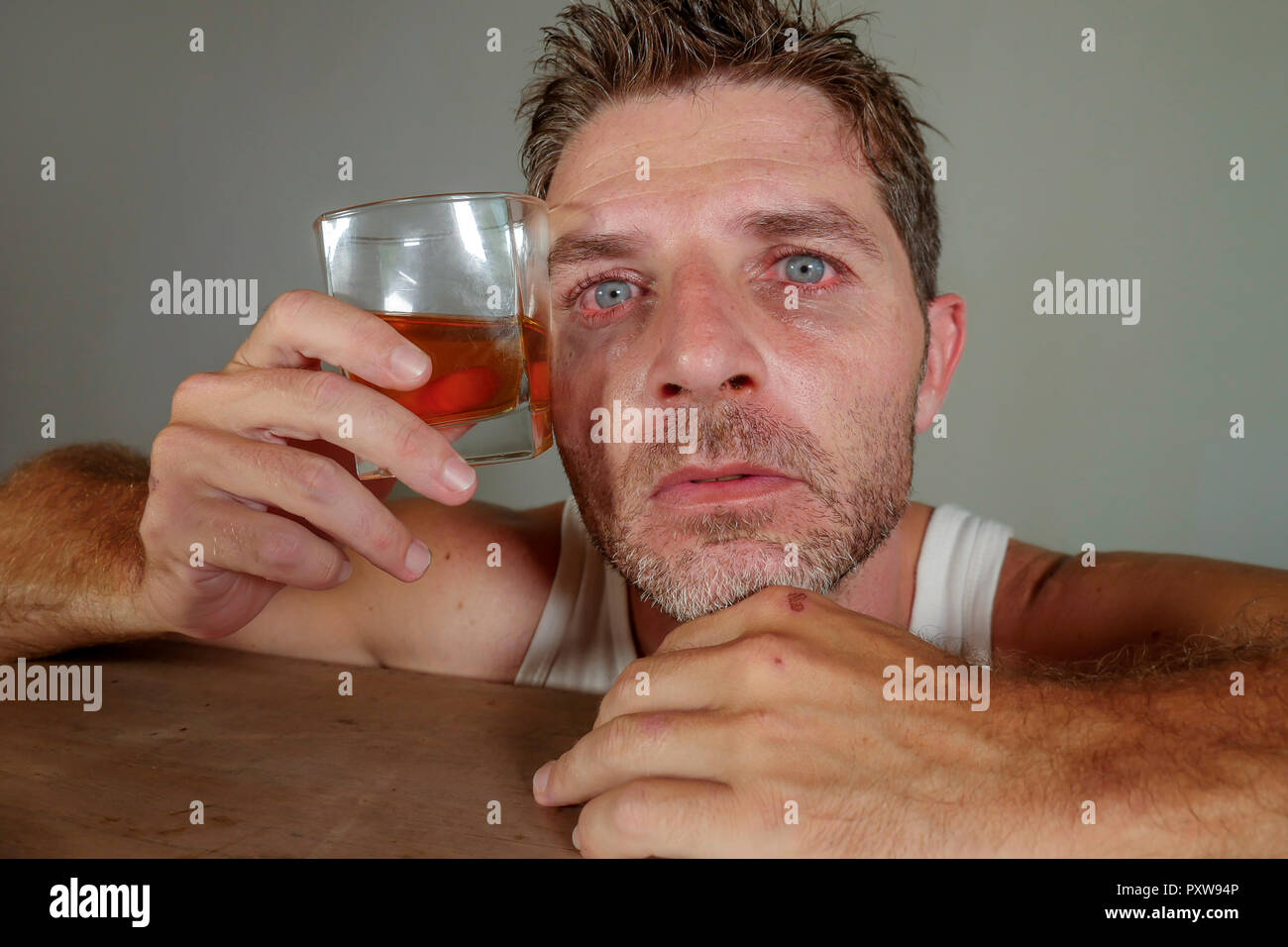 young drunk and pissed alcoholic man wasted wearing dirty singlet drinking whiskey glass ...