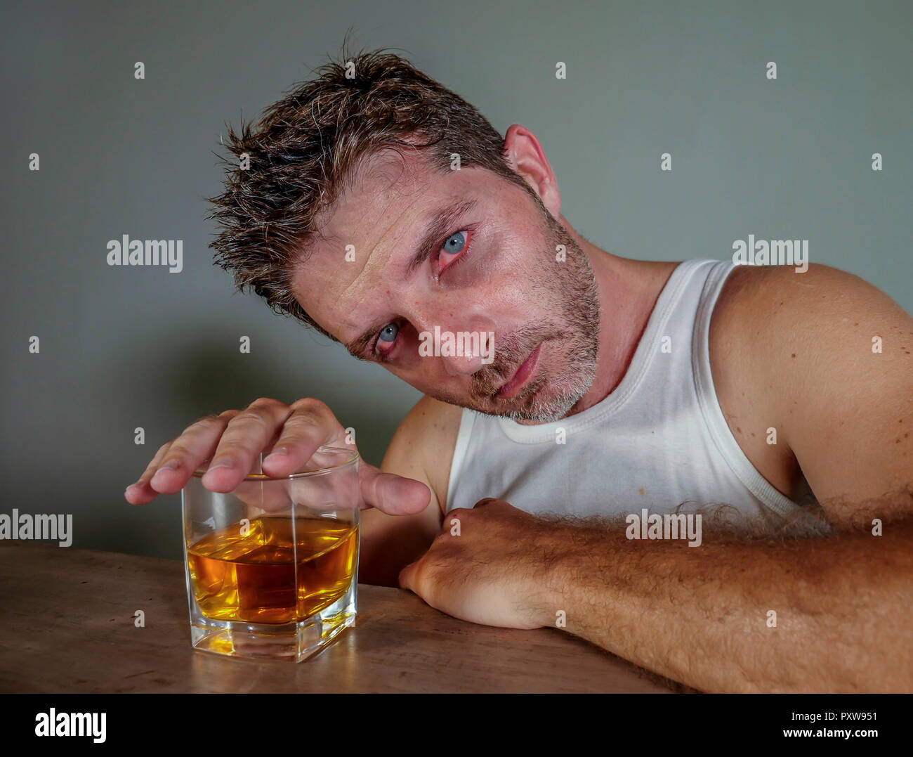 young drunk and pissed alcoholic man wasted wearing dirty singlet drinking whiskey glass ...