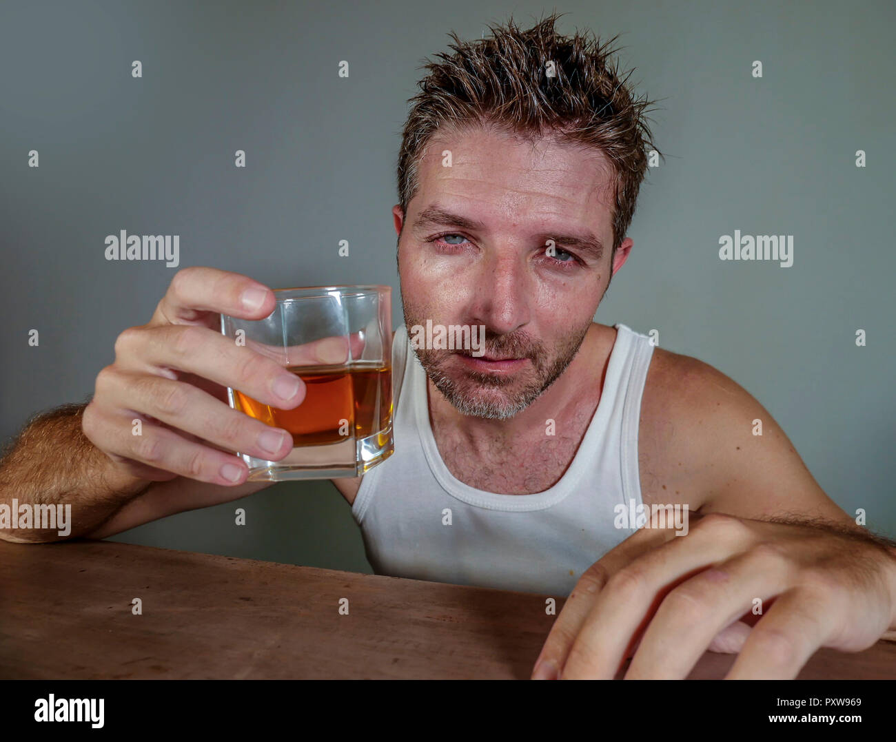 young drunk and pissed alcoholic man wasted wearing dirty singlet drinking whiskey glass ...