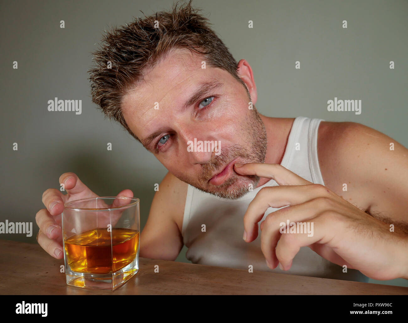 young drunk and pissed alcoholic man wasted wearing dirty singlet drinking whiskey glass ...