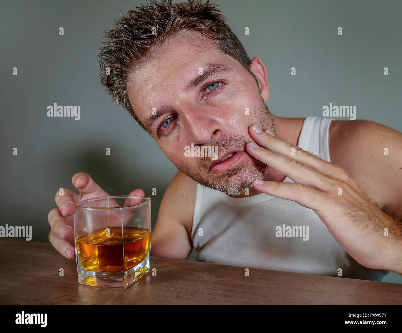 young drunk and pissed alcoholic man wasted wearing dirty singlet drinking whiskey glass ...