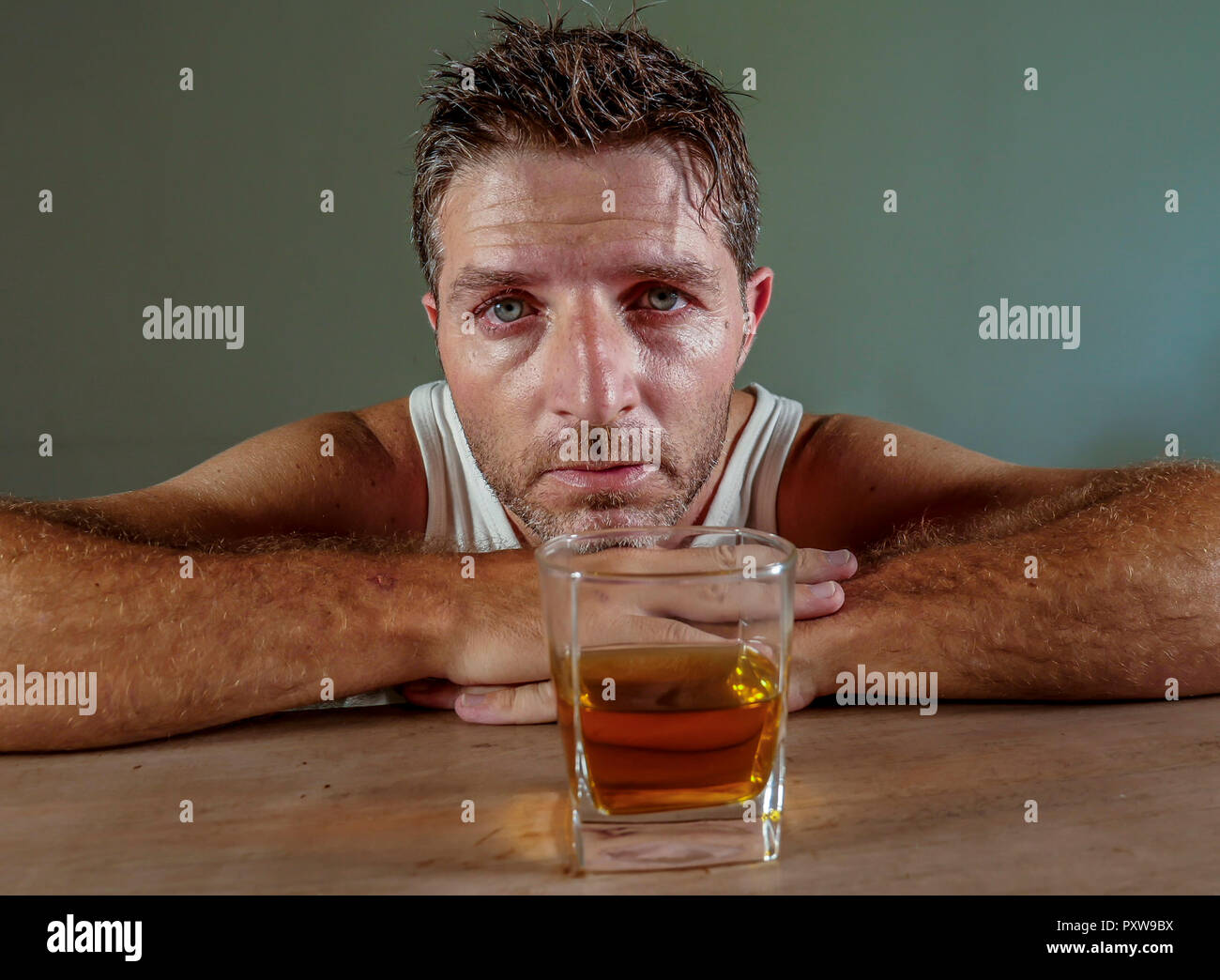 young wasted and depressed alcohol addict man in singlet drinking glass ...