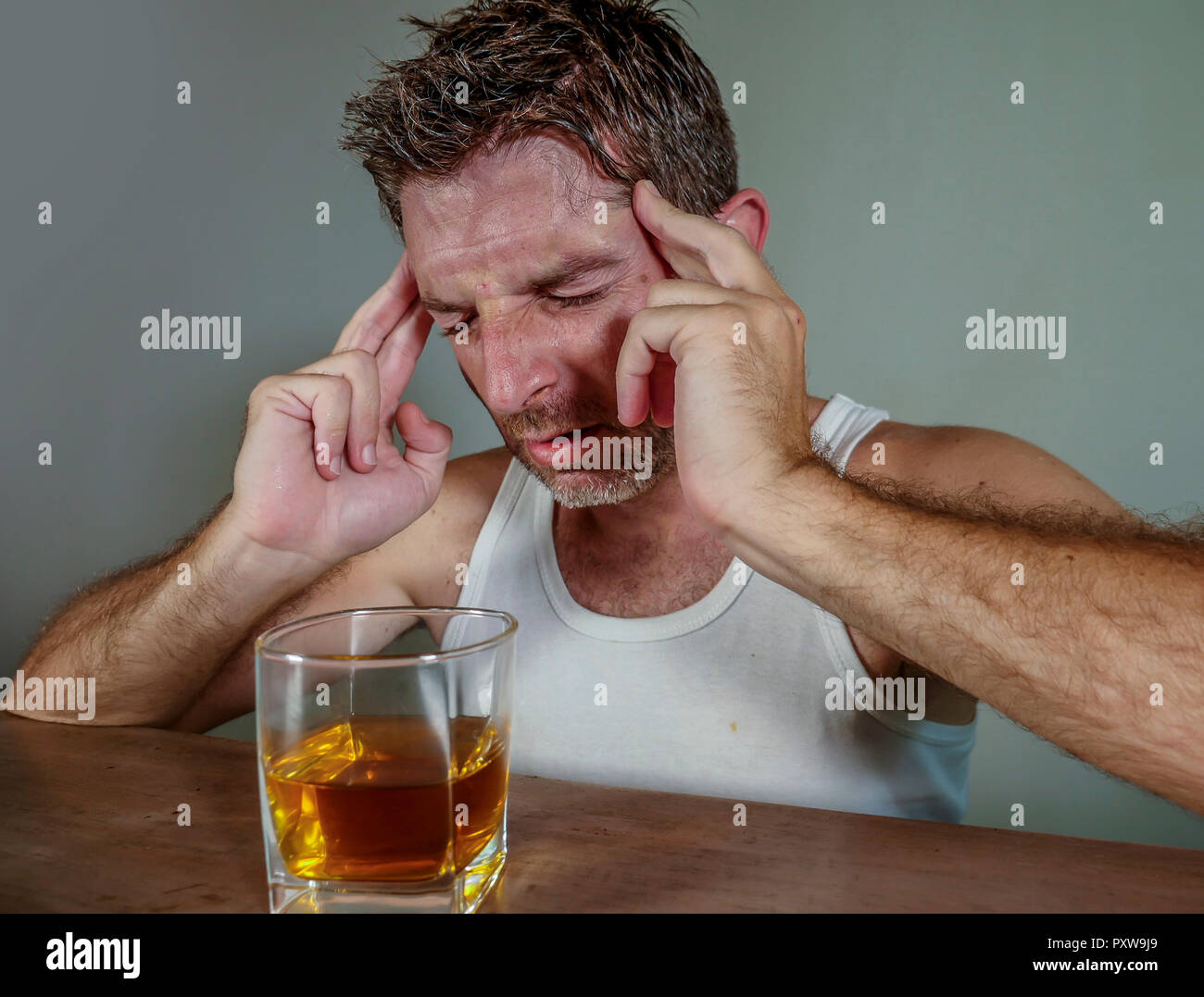 young wasted and depressed alcohol addict man in singlet drinking glass ...