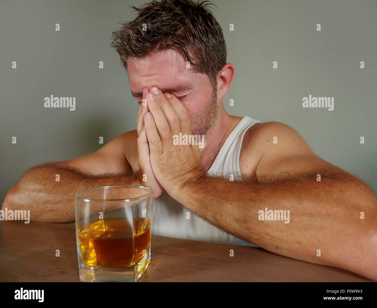 young wasted and depressed alcohol addict man in singlet drinking glass ...