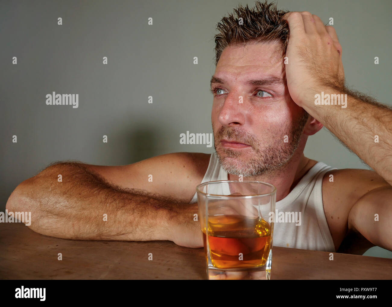 young wasted and depressed alcohol addict man in singlet drinking glass ...