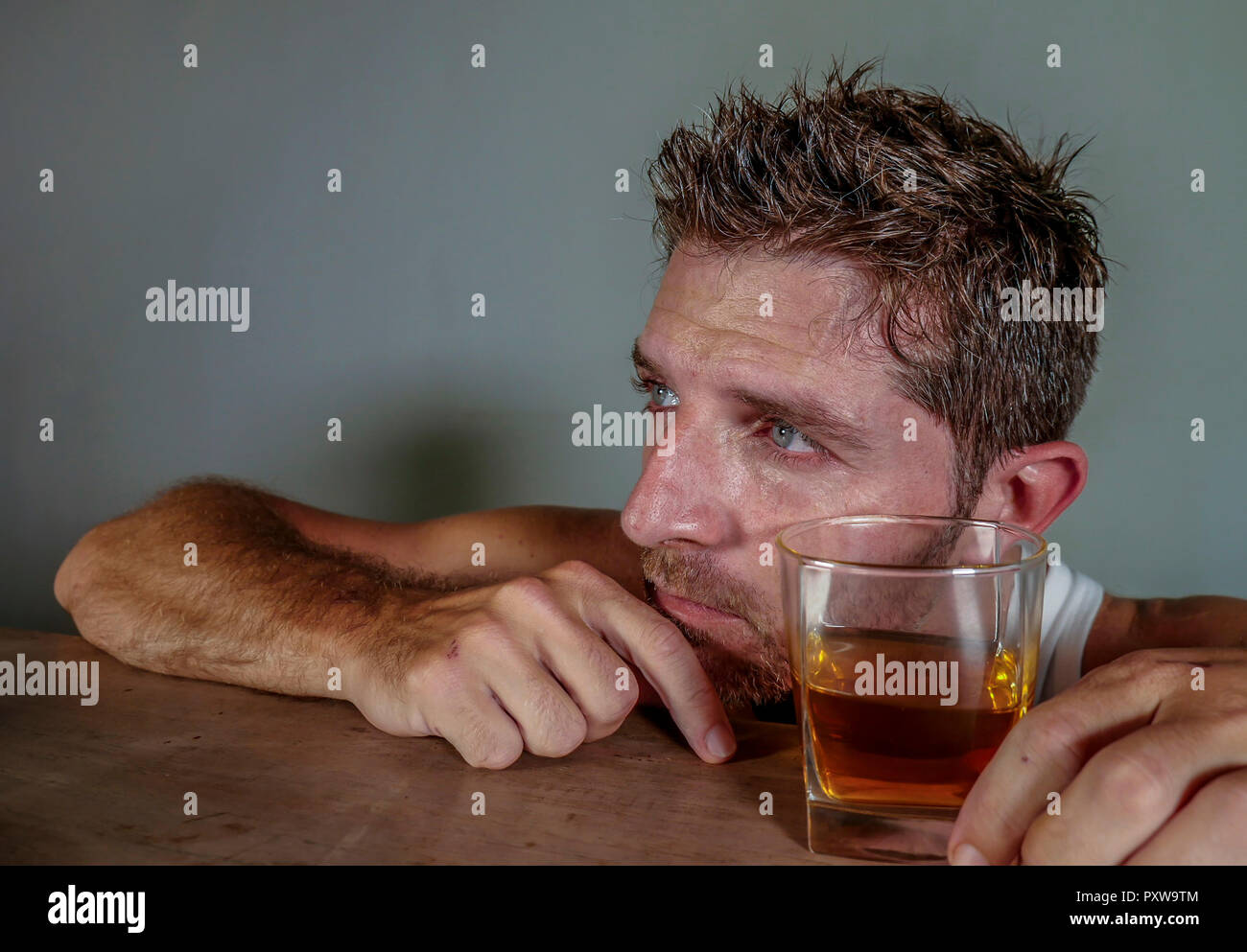 young wasted and depressed alcohol addict man in singlet drinking glass ...