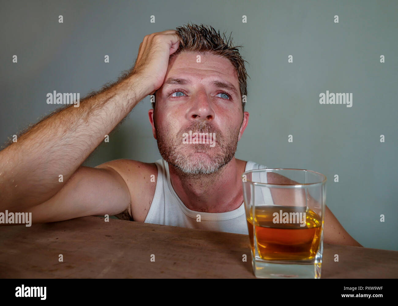 young wasted and depressed alcohol addict man in singlet drinking glass ...