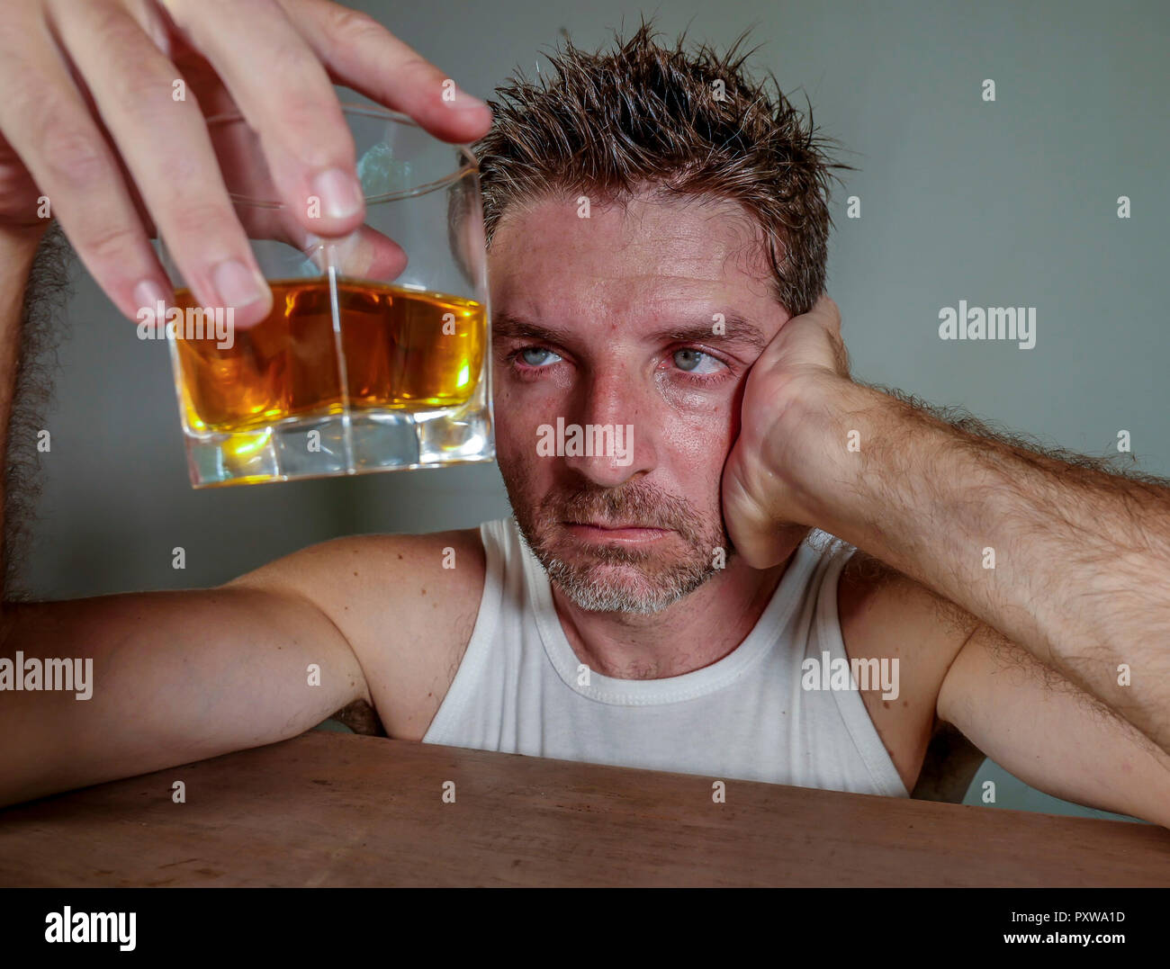 young wasted and depressed alcohol addict man in singlet drinking glass ...