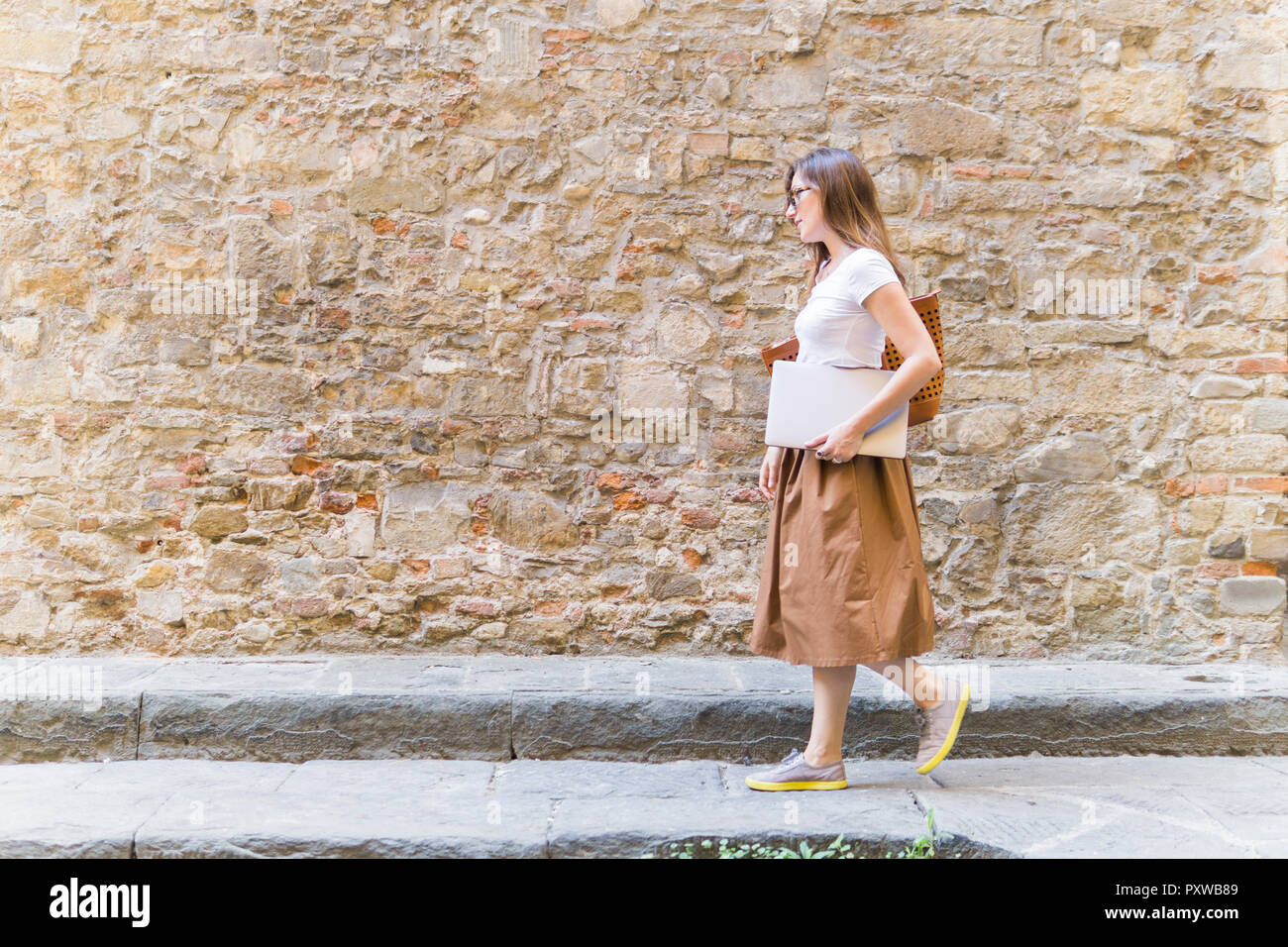 Woman walking along stone wall carrying laptop hi-res stock photography ...