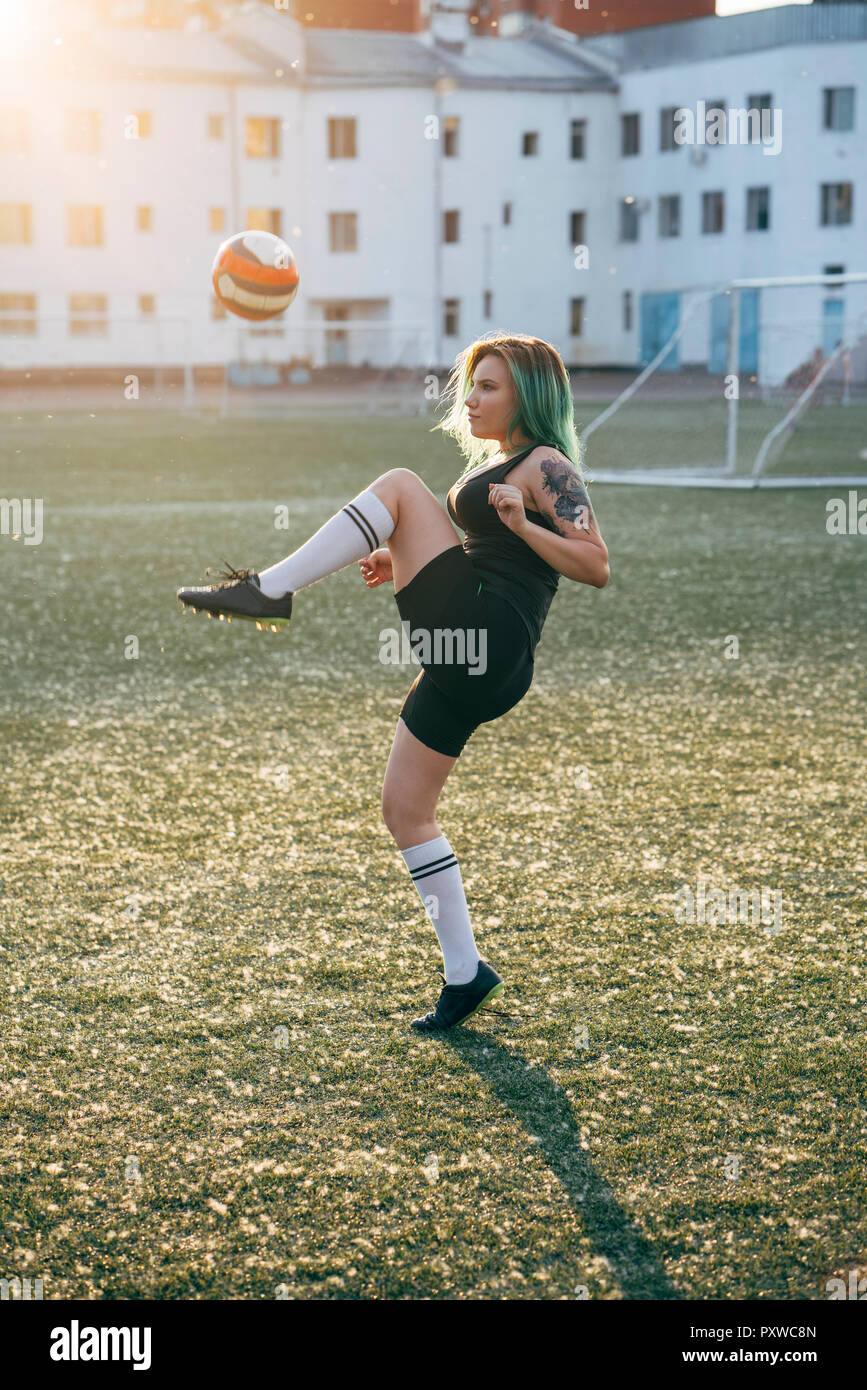 Young woman playing football on football ground balancing the ball ...