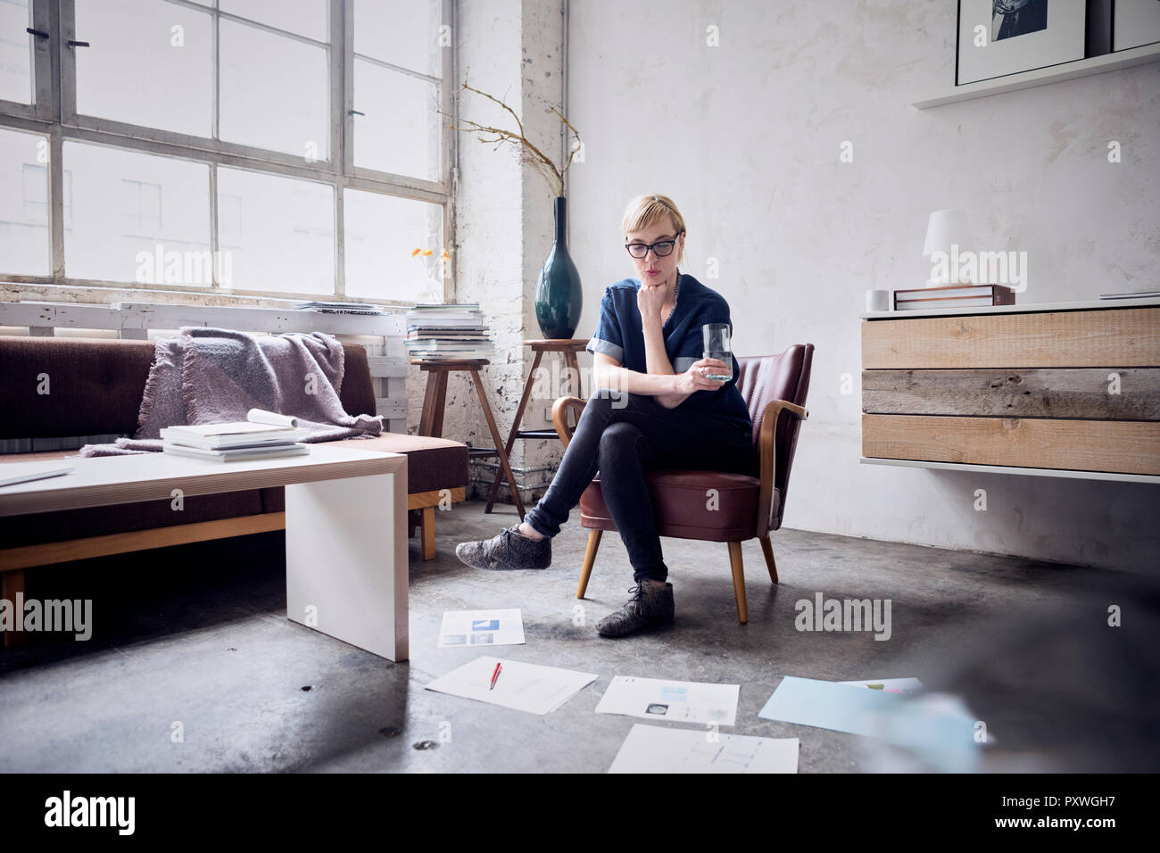 Woman sitting on arm chair in loft looking at papers on the floor Stock ...