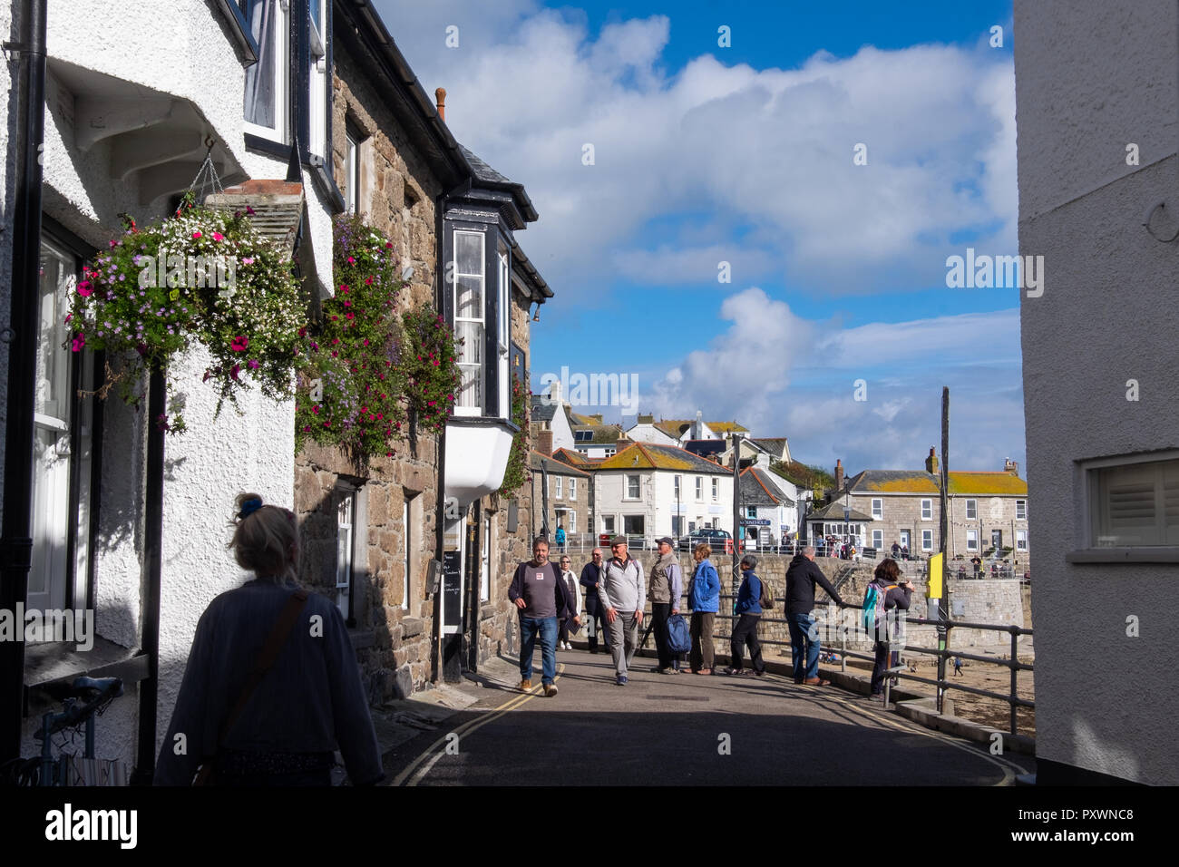 Harbourside, narrow street in the sunshine of Mousehole with tourists ...