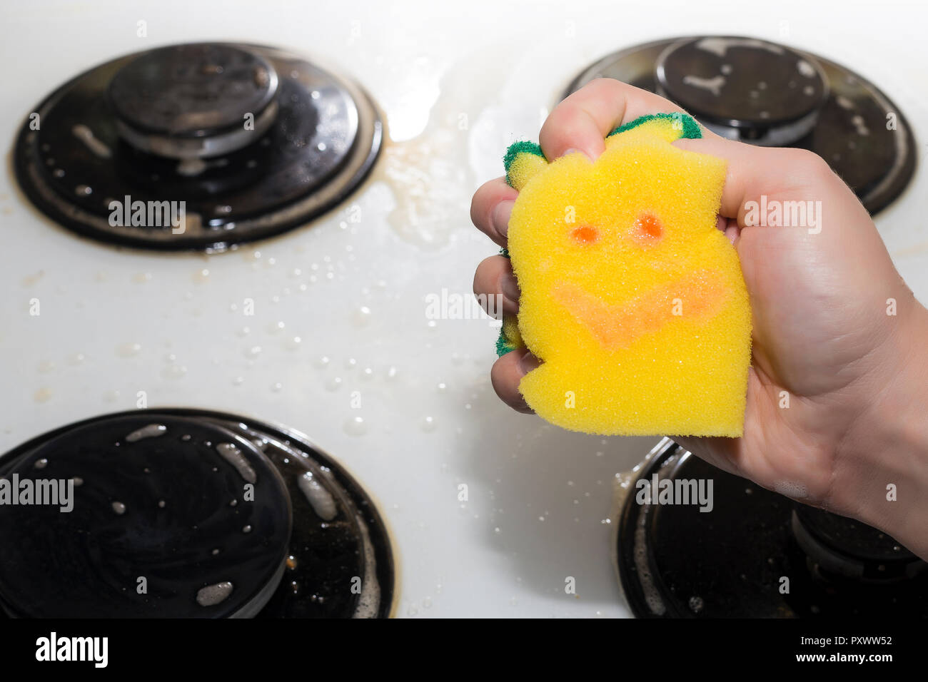 yellow sponge in hand with painted smile, for dishes on dirty gas stove ...
