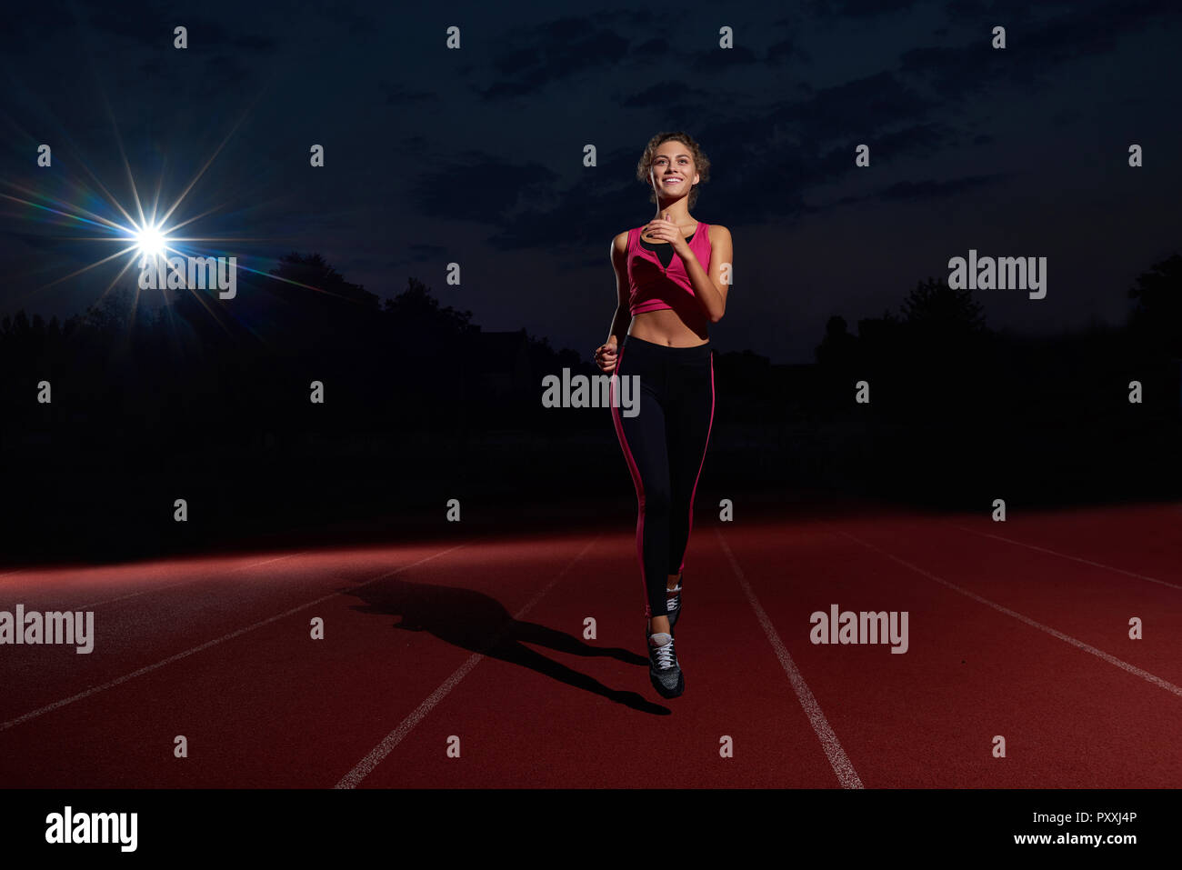 Positivity and happy young woman in sport wear running forward on track ...