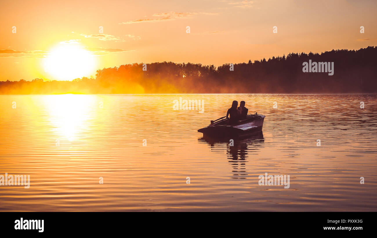 Couple in love ride in a rowing boat on the lake during sunset ...