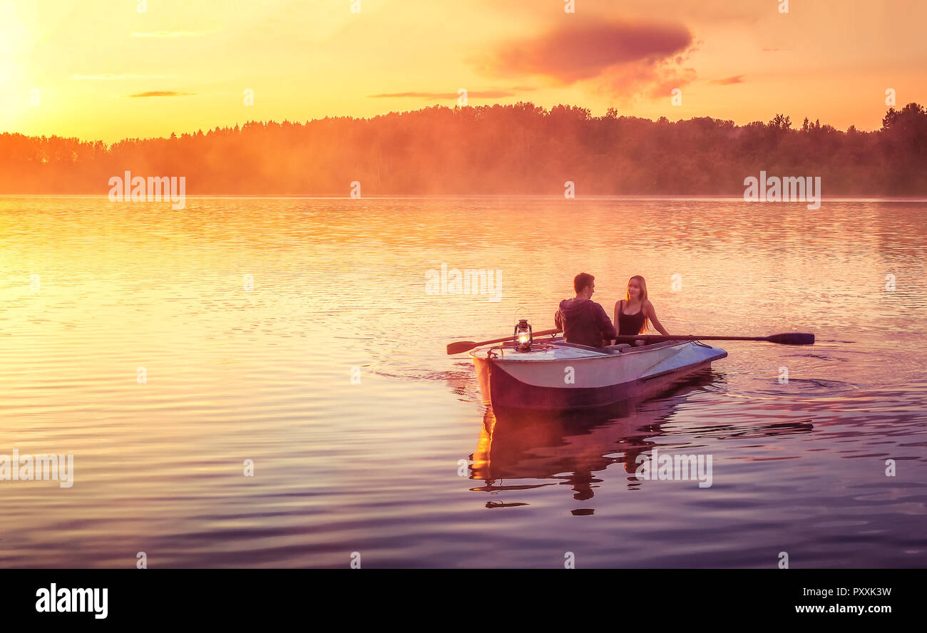 Couple in love ride in a rowing boat on the lake during sunset ...