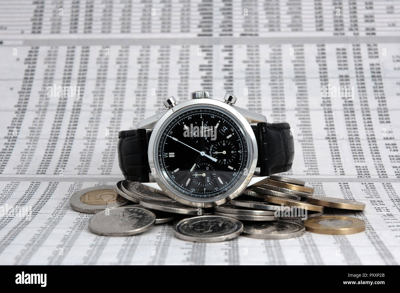 High class male watch lying on coins, stock market quotes in background ...