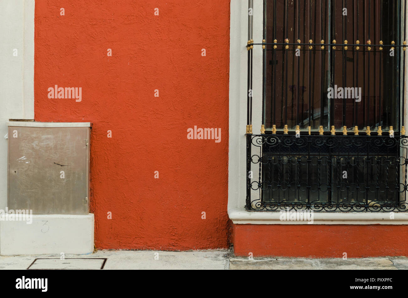 Window with black bars and a metal box on one side on an orange wall ...
