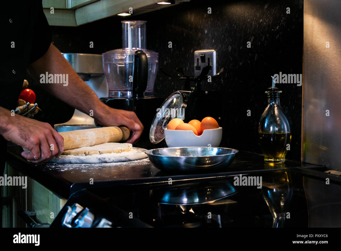 Arms of male chef using rolling pin to roll out pastry into a dish ...