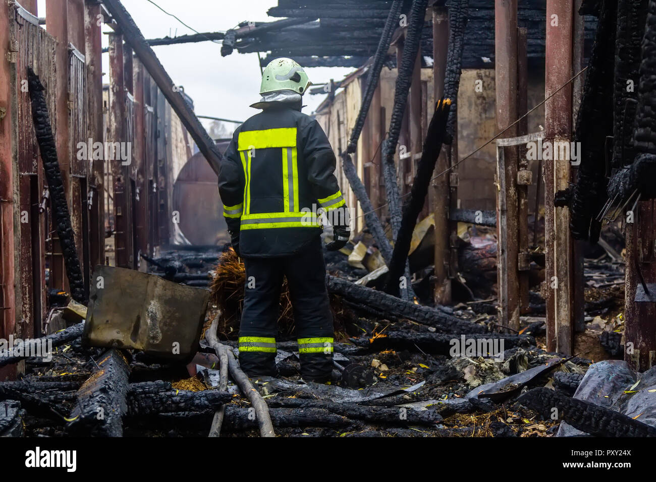 firefighter stands among the ruins of a fully burned farm, disaster ...