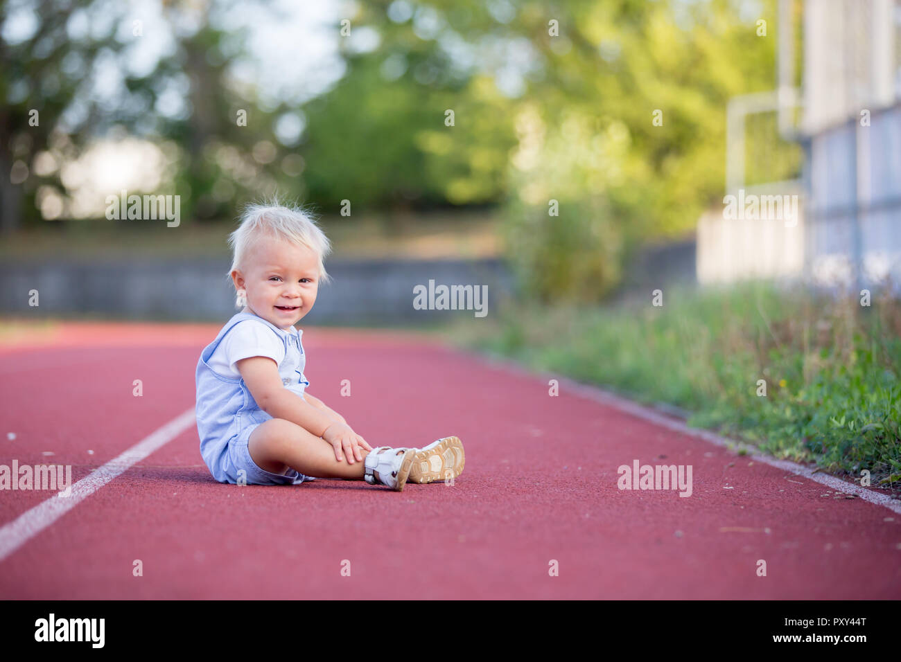 Cute toddler baby boy on a running path on a stadium, playing Stock ...