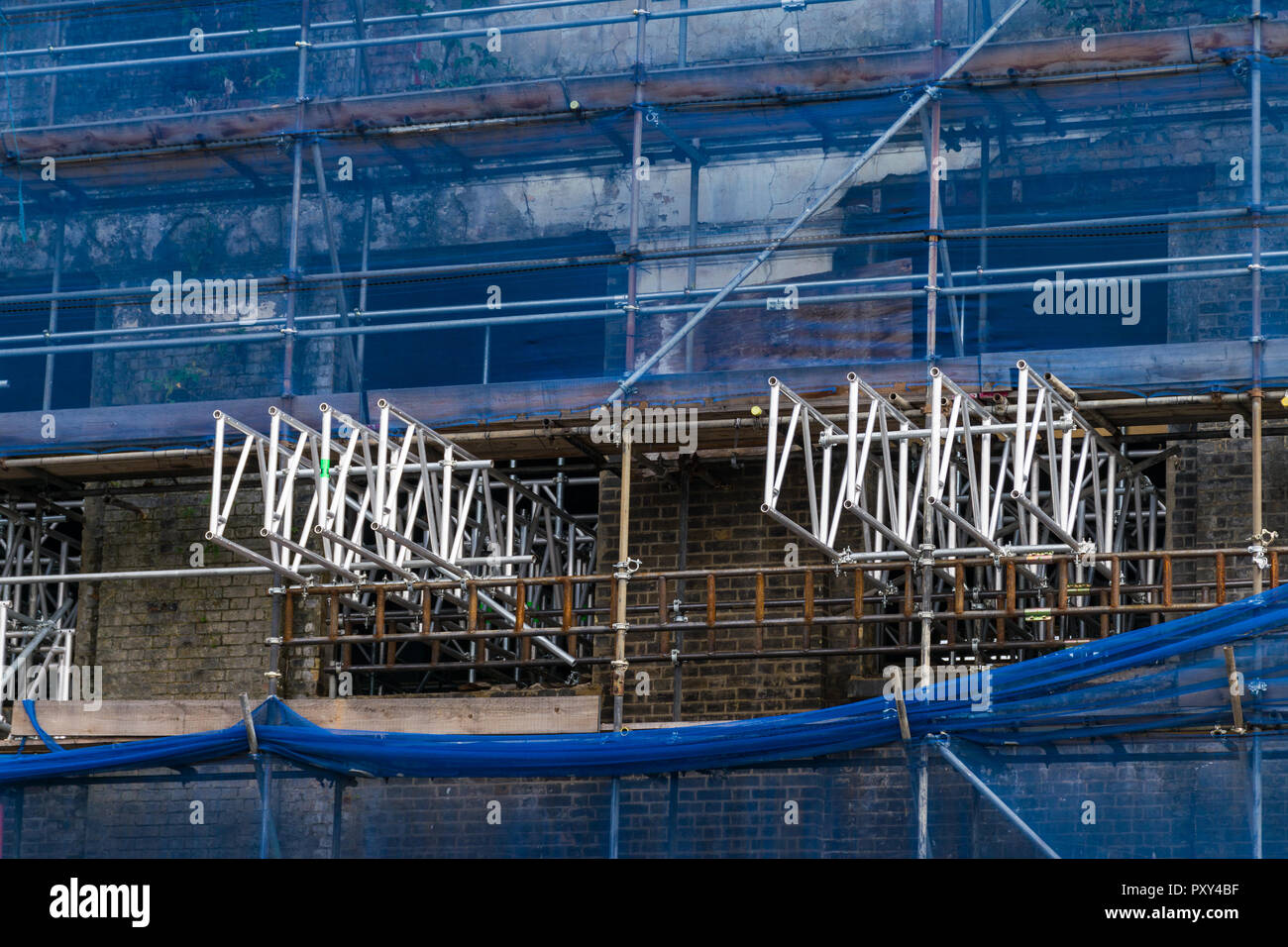 Scaffolding, blue netting and steel reinforcement on an old brick ...