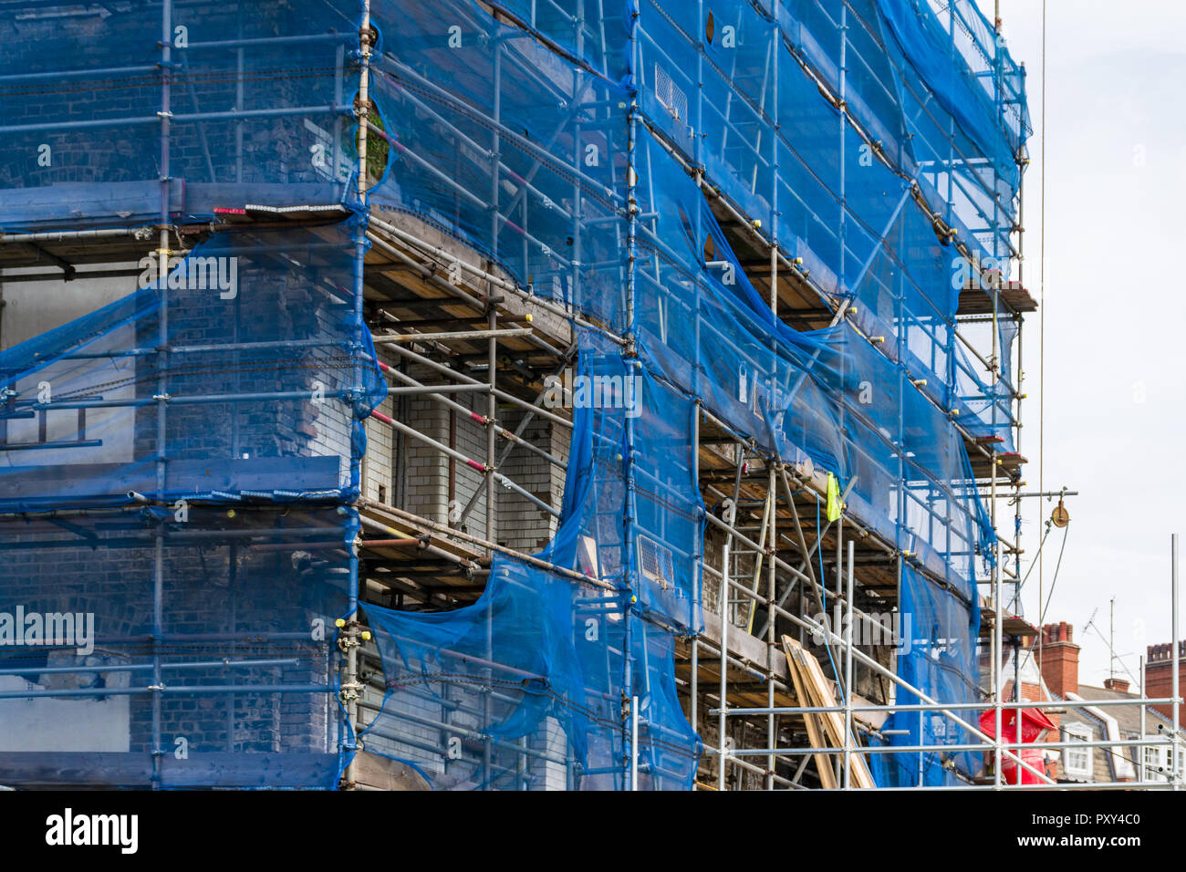 Scaffolding, blue netting and steel reinforcement on an old brick ...