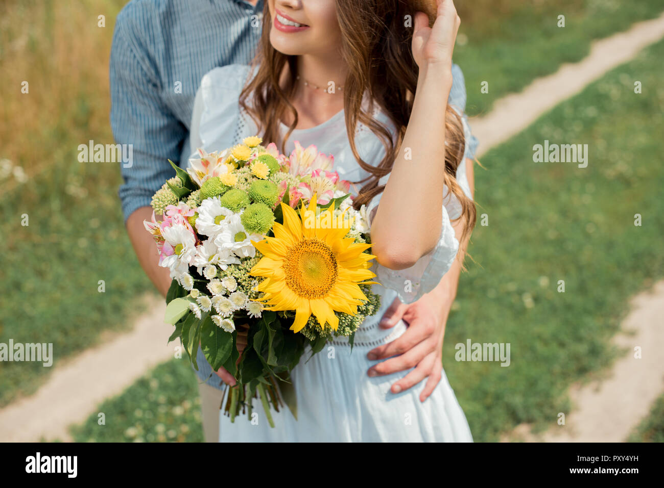 partial view of man hugging smiling girlfriend with bouquet of wild ...
