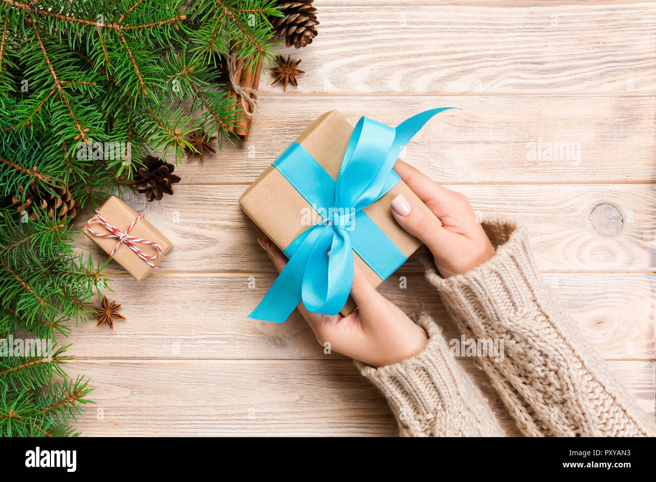 female hands hold wrapping christmas gift box with blue ribbon on broen ...