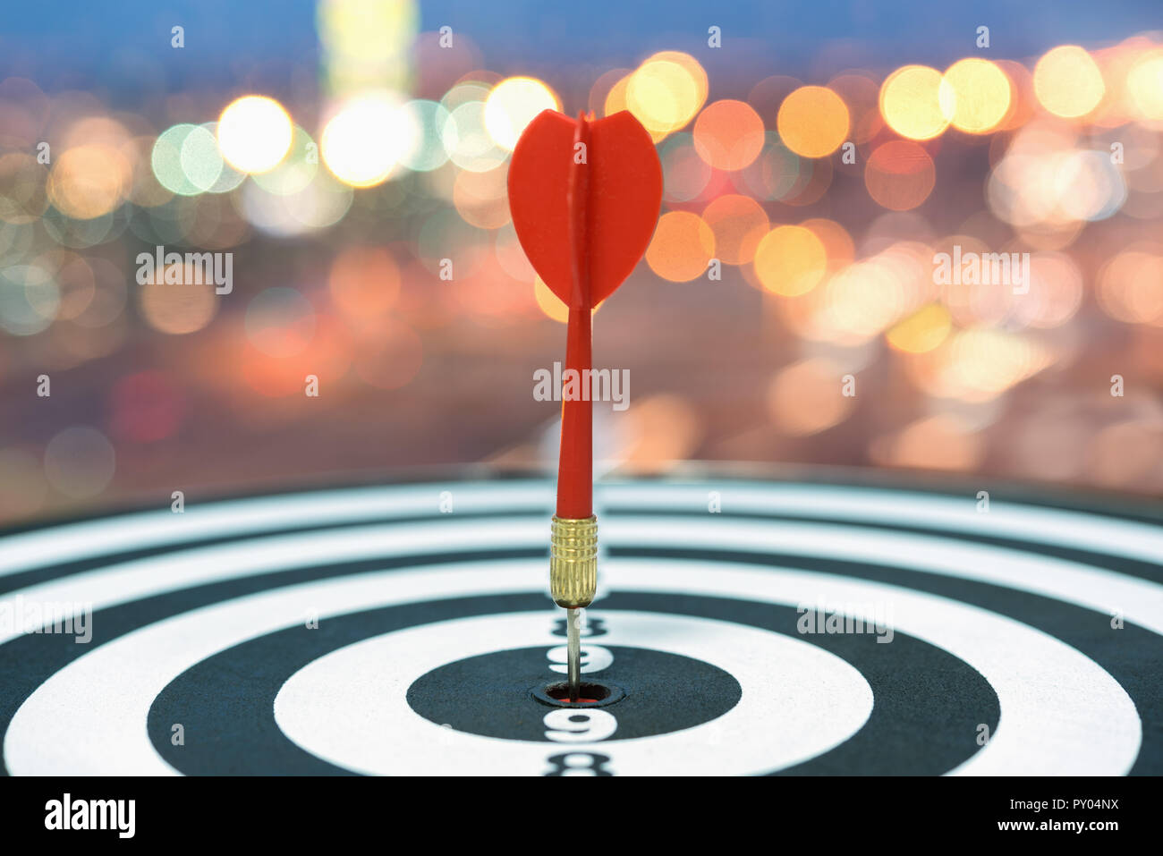Red dart target arrow hitting on bullseye over blurred bokeh light ...