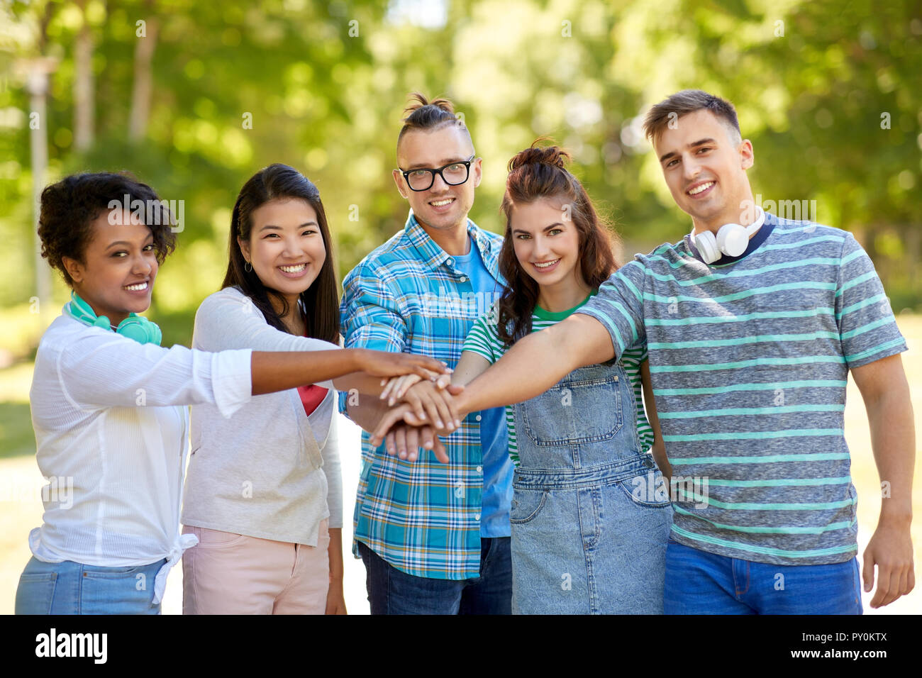 happy smiling friends stacking hands in park Stock Photo - Alamy