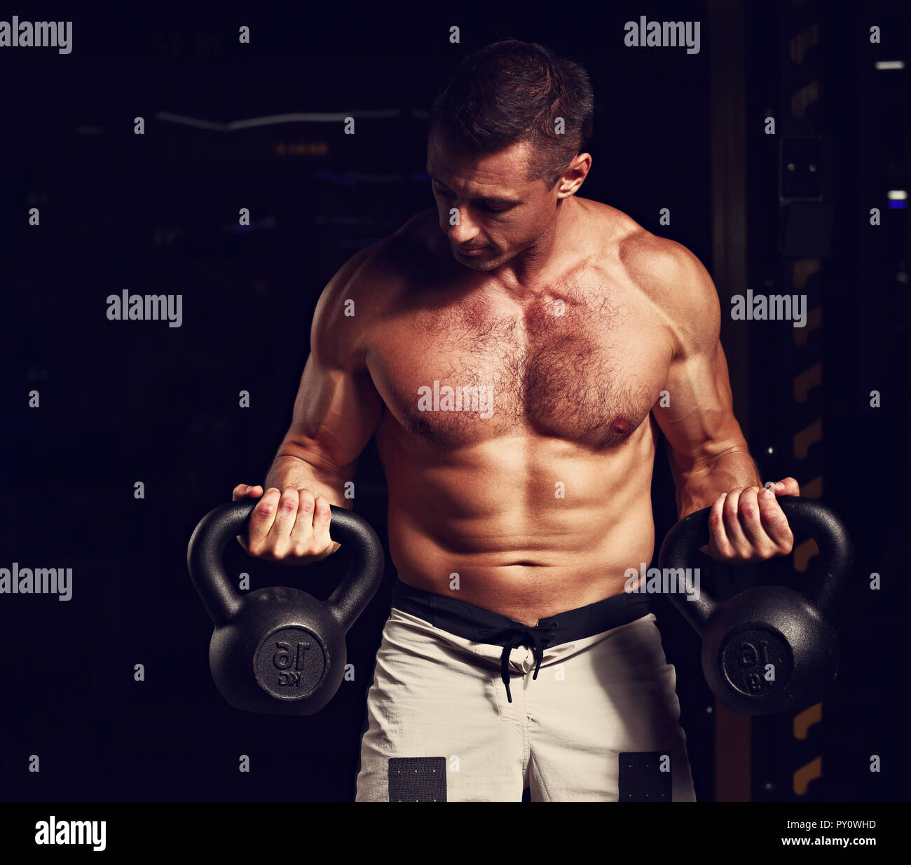 Strong athletic man doing the exercises with kettlebells on dark shadow ...