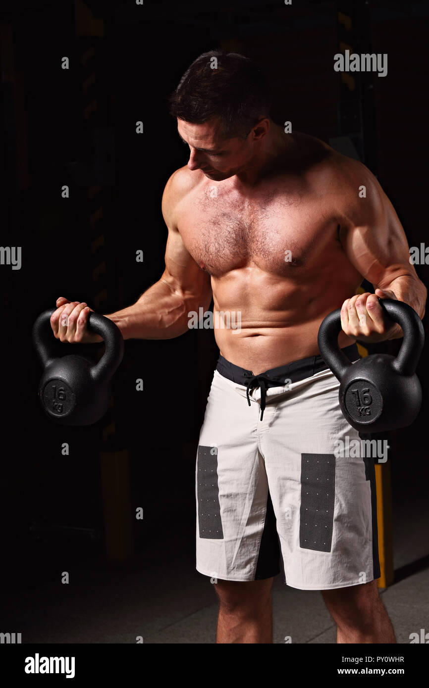 Handsome strong man doing the exercises with kettlebells on dark shadow ...