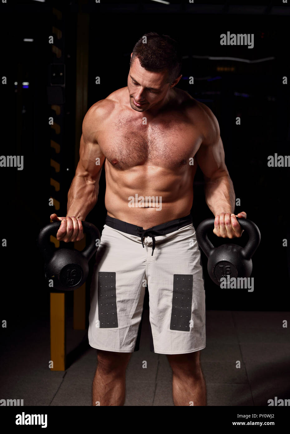 Handsome strong man doing the exercises with kettlebells on dark shadow ...