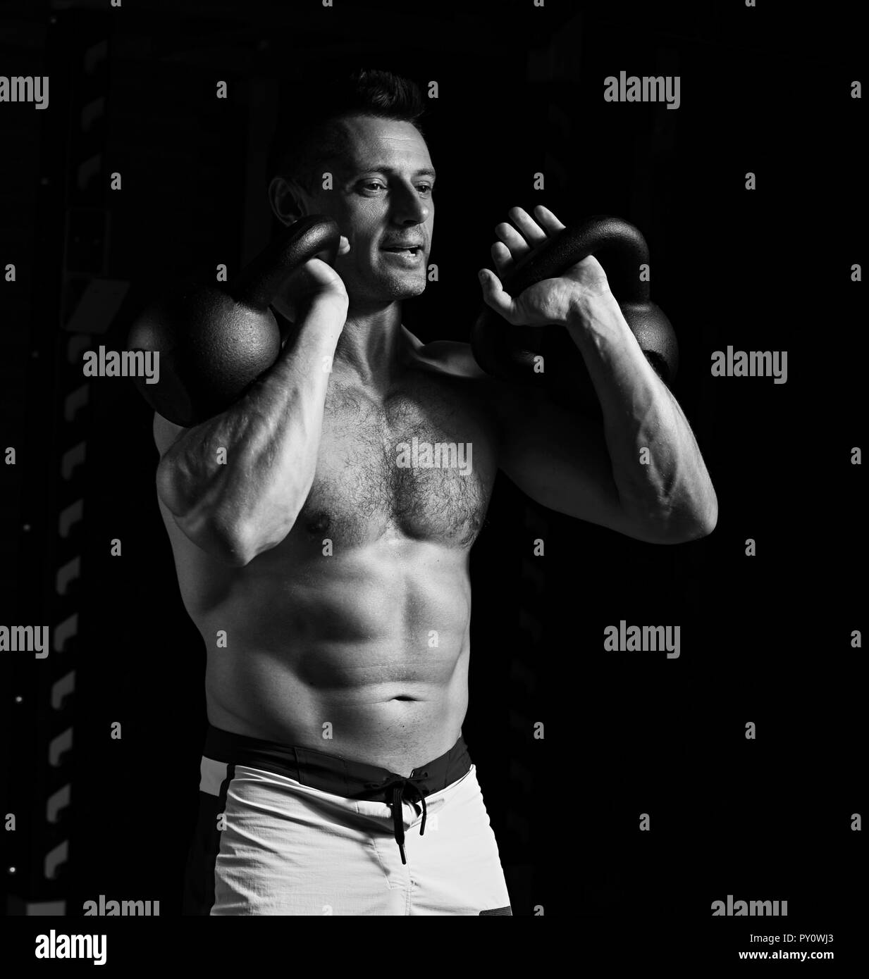 Handsome strong man doing the exercises with kettlebells on dark shadow ...