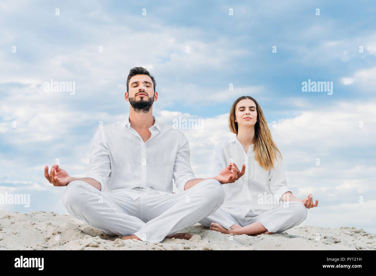 calm young couple meditating while sitting on sandy dune in lotus pose ...