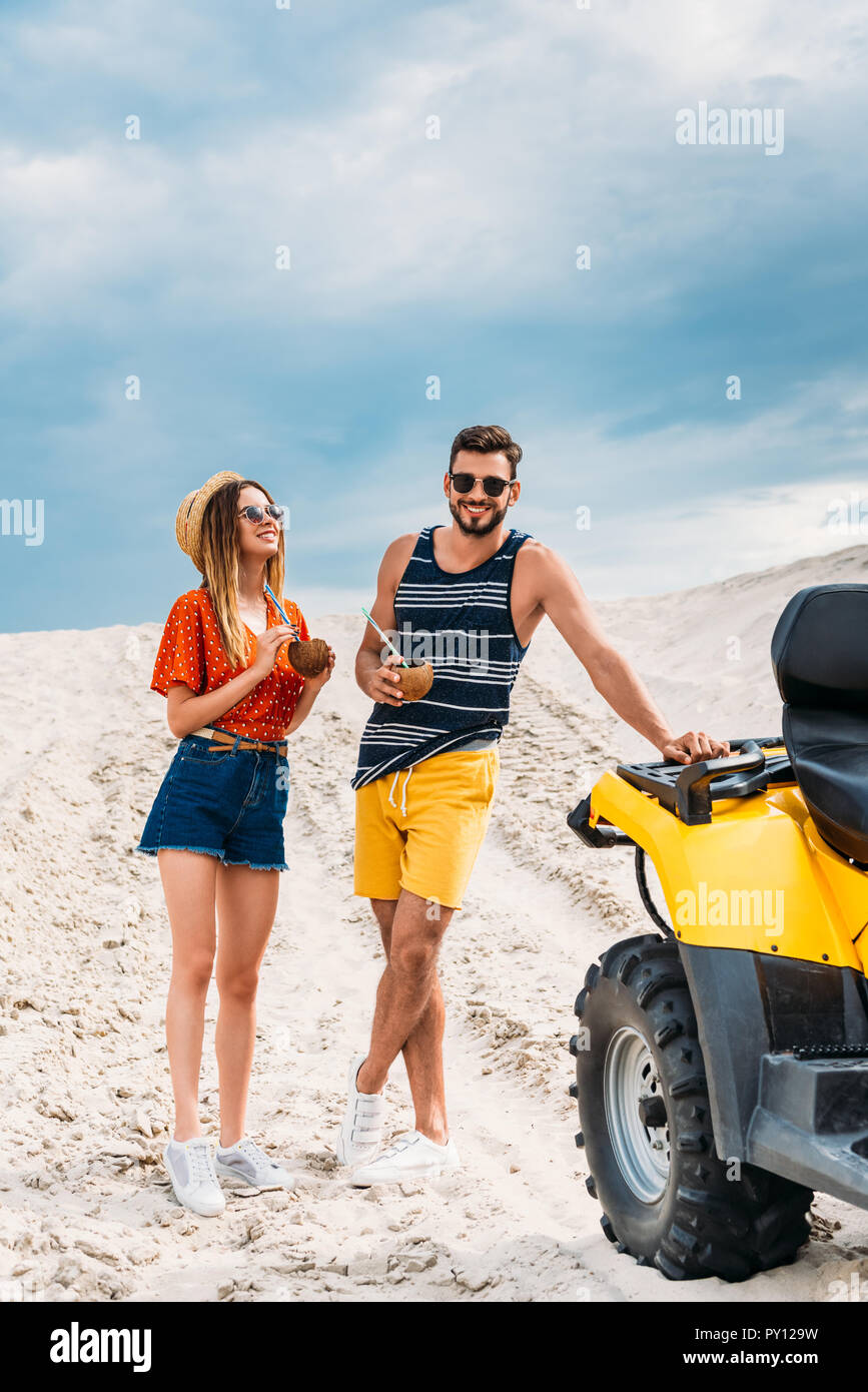 smiling young couple with atv and coconut cocktails in desert Stock ...